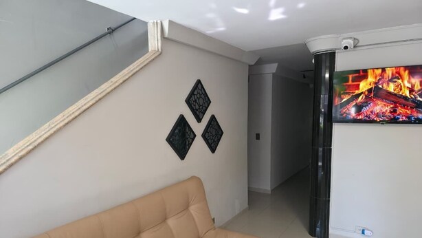 Sala de estar com sofá bege, escada e televisão na parede exibindo uma lareira.