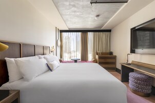 Quarto de hotel com cama grande, uma escrivaninha, televisão e janela com cortinas.