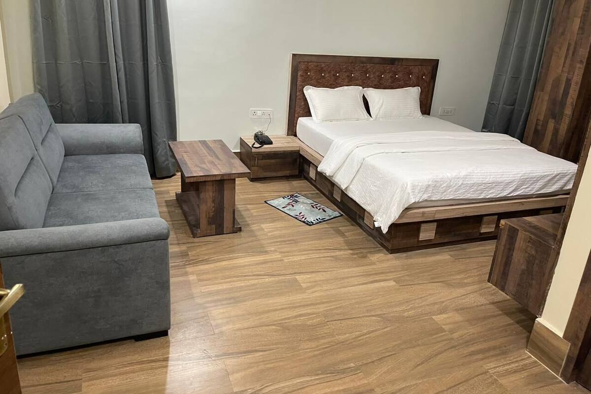 Quarto com cama, sofá, mesa de cabeceira e piso de madeira.