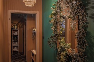 Um corredor com uma porta de madeira, uma prateleira com toalhas e uma parede decorada com plantas.