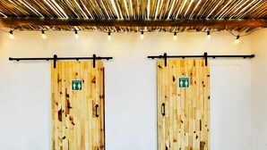 Duas portas de madeira com placas de "TOILETS", teto de bambu e luzes de cordão.