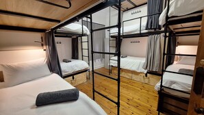 Quarto com beliches, piso de madeira e roupa de cama branca.