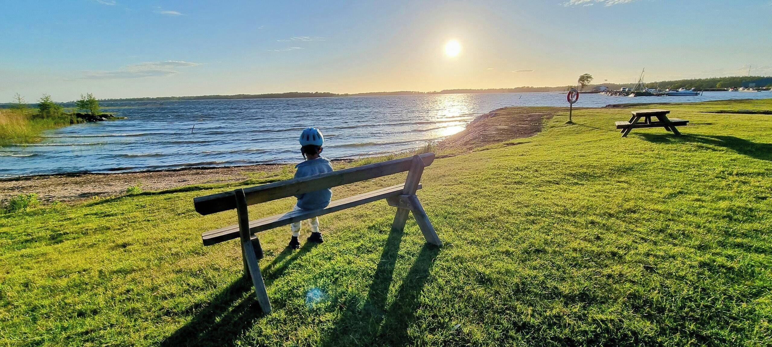 Um banco à beira de um lago, com uma mesa de piquenique e uma placa ao fundo.