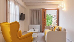 Quarto com poltrona amarela, sofá branco, mesa pequena, televisão e vista para o exterior.