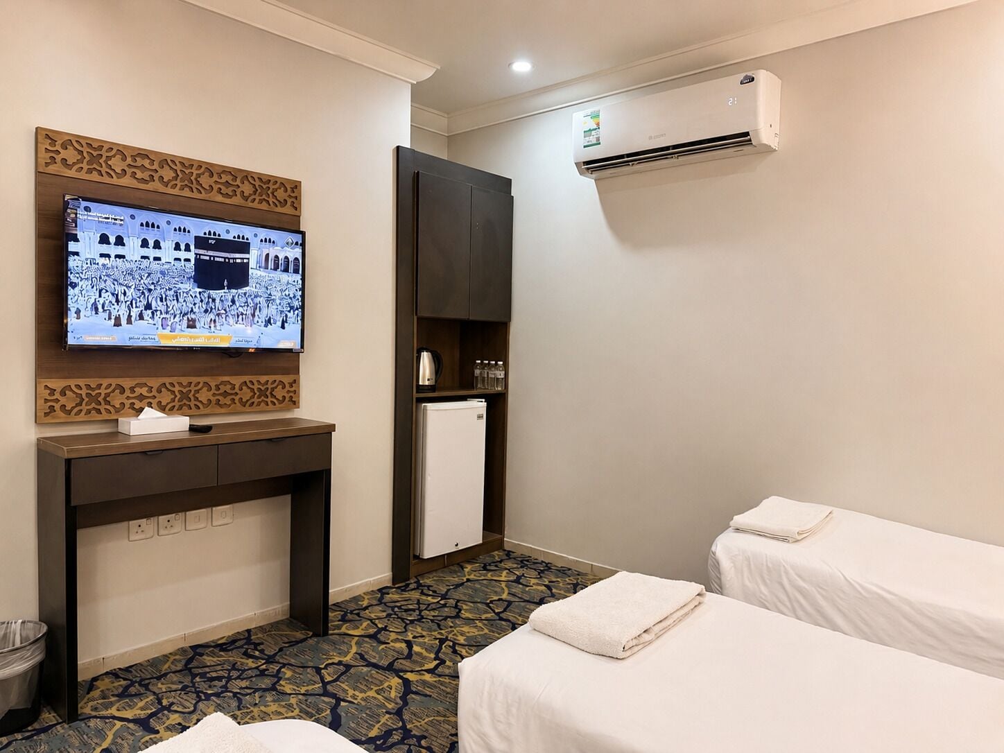 Quarto de hotel com televisão, ar condicionado, minibar, carpete estampado e duas camas.