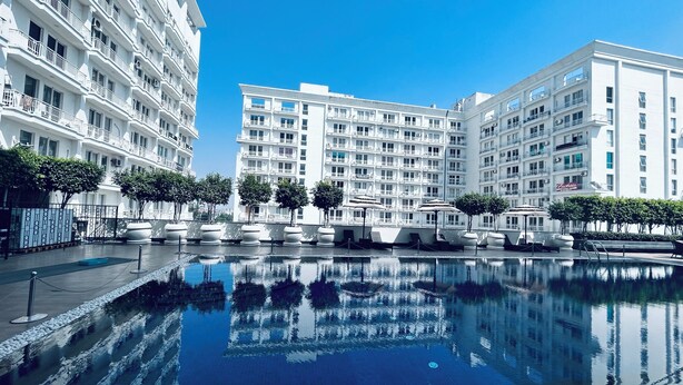 Um hotel moderno com piscina central, rodeado por edifícios brancos e árvores.
