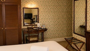 Quarto de hotel com cama, escrivaninha com cadeira, espelho, luminária pendente e guarda-roupa de madeira.