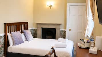 Quarto de hotel com cama, poltrona, escrivaninha com luminária, lareira e televisão.