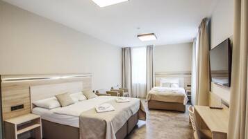 Quarto de hotel com uma cama grande, uma cama menor, uma escrivaninha e uma televisão.