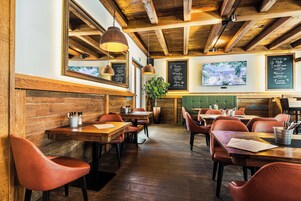 Interior de restaurante com vigas de madeira, mesas, cadeiras e um quadro de menu.