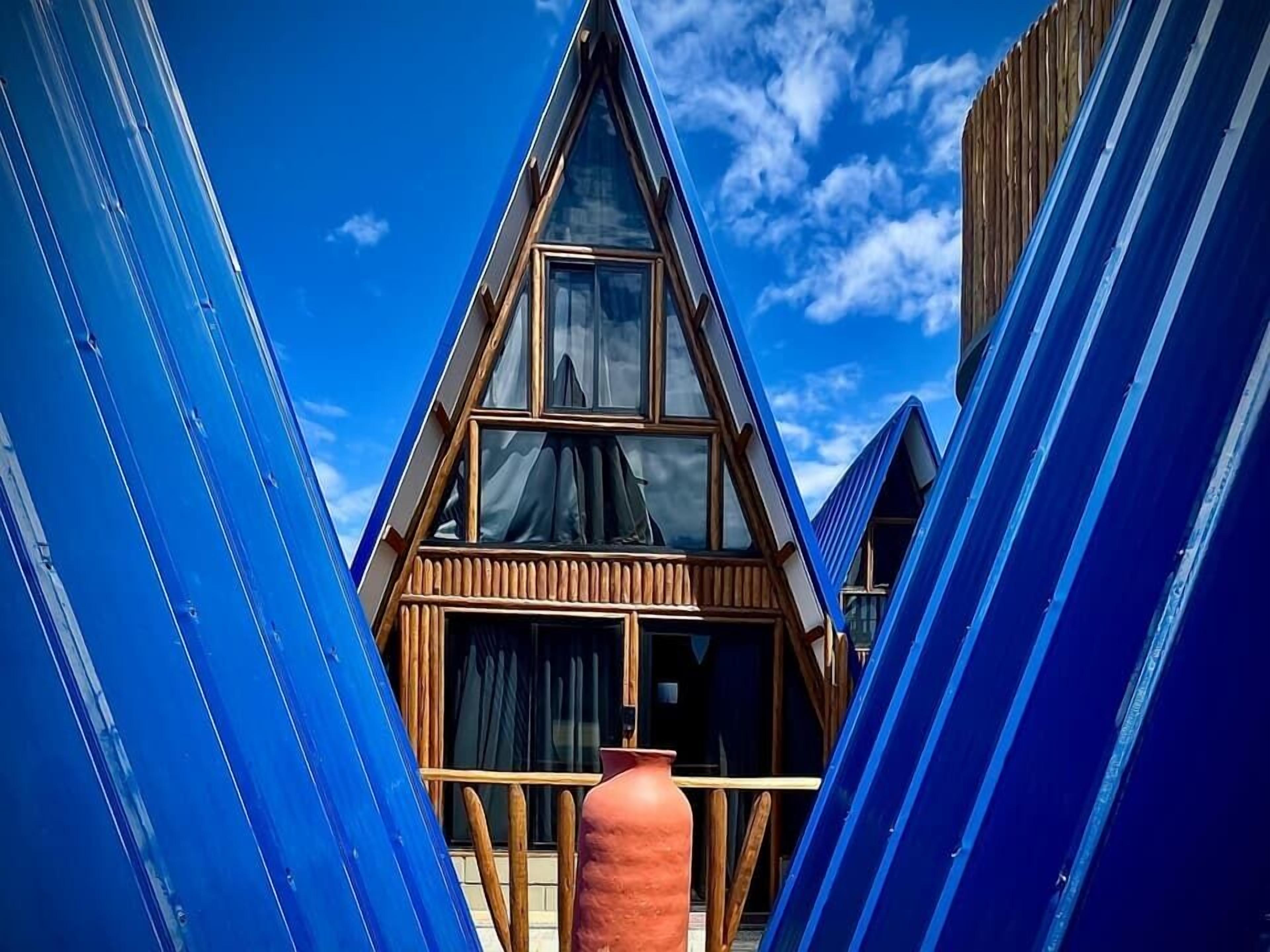 Um edifício triangular com fachada de madeira e janelas amplas, cercado por estruturas azuis.