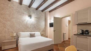 Quarto com cama, mesas de cabeceira, um apoio para objetos, uma cadeira e uma cozinha com bancada e eletrodomésticos.