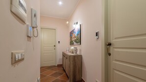 Um corredor com uma porta, um telefone fixado na parede, um interruptor de luz e um quadro.
