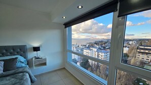 Quarto com uma janela grande, cama, mesa de cabeceira e abajur.