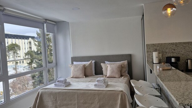 Quarto de hotel moderno com uma cama grande, cozinha e área de estar com banquetas.