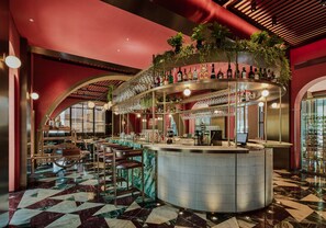 Uma área de bar com balcão curvo, diversas opções de assento e uma variedade de garrafas e copos expostos.