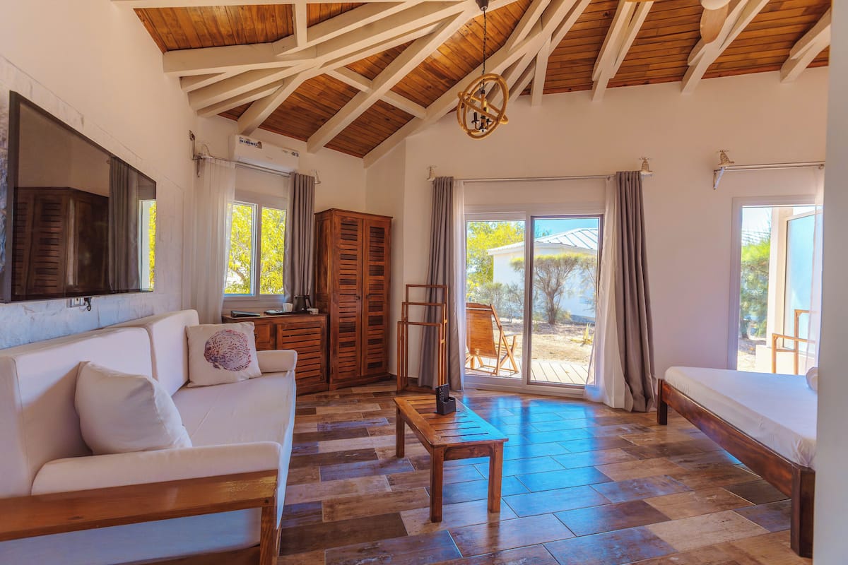 Uma sala de estar ampla com teto de madeira, um sofá, uma mesa de centro e uma porta de vidro deslizante que dá para uma área externa.