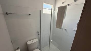 Casa de banho com cabine de duche em vidro, sanita e barra de toalhas.