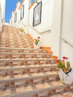 Uma escadaria com azulejos estampados que leva a um edifício com paredes brancas e detalhes em laranja.
