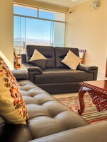 Uma sala de estar moderna com um sofá de couro, uma manta estampada e uma mesa de centro de madeira.