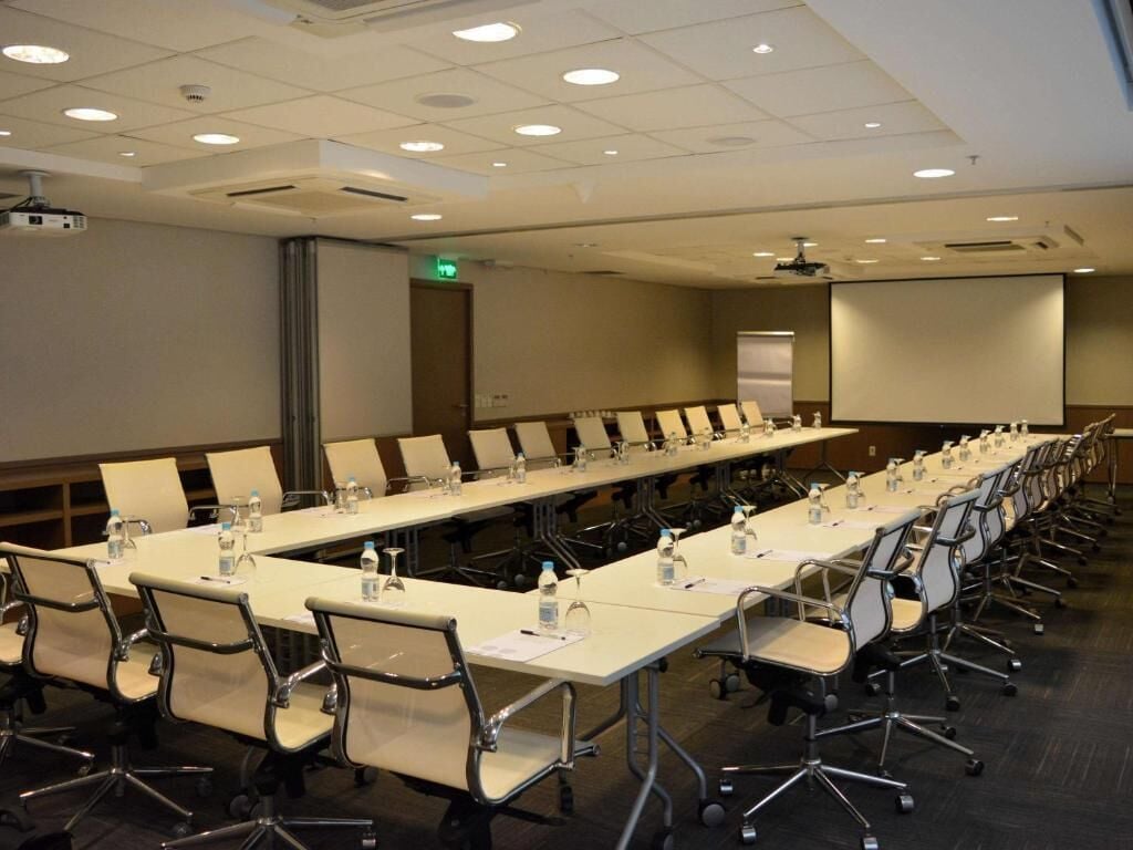 Uma sala de conferências com uma mesa comprida, cadeiras e uma tela de projeção.