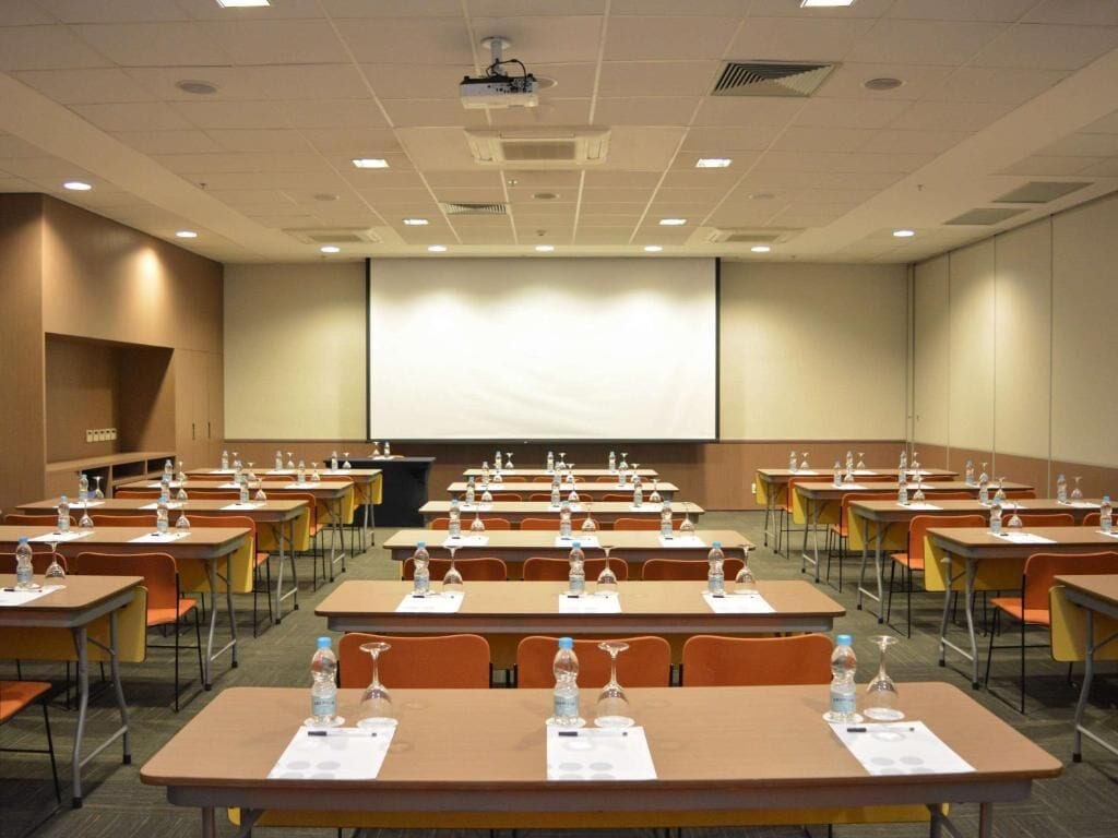 Uma sala de conferências com fileiras de mesas, cada uma com uma garrafa de água e um copo.
