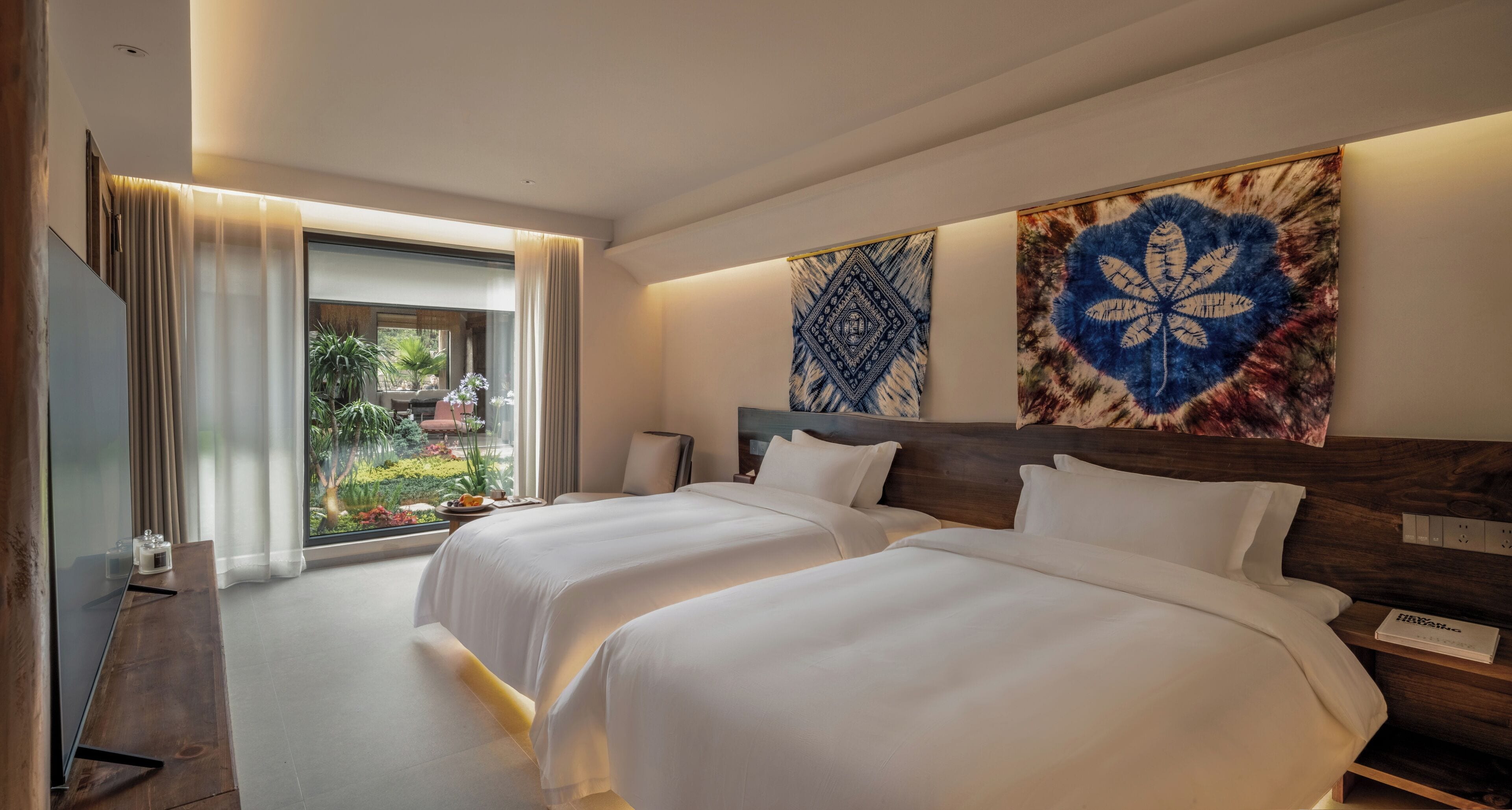 Quarto de hotel com duas camas, uma janela grande com cortinas e uma obra de arte na parede.
