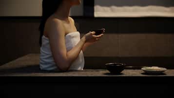 Uma pessoa de toalha sentada perto de uma mesa com uma tigela e um prato, segurando um smartphone.