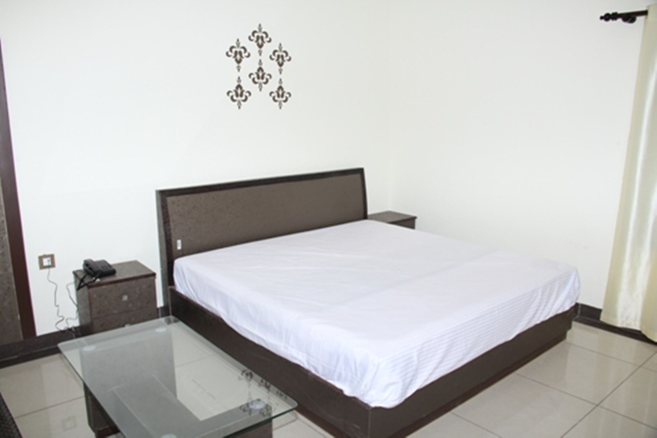 Quarto com uma cama, mesa de cabeceira e uma mesa de vidro.