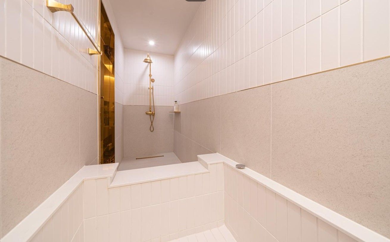 Casa de banho com paredes em azulejos brancos, chuveiro dourado e banheira branca.