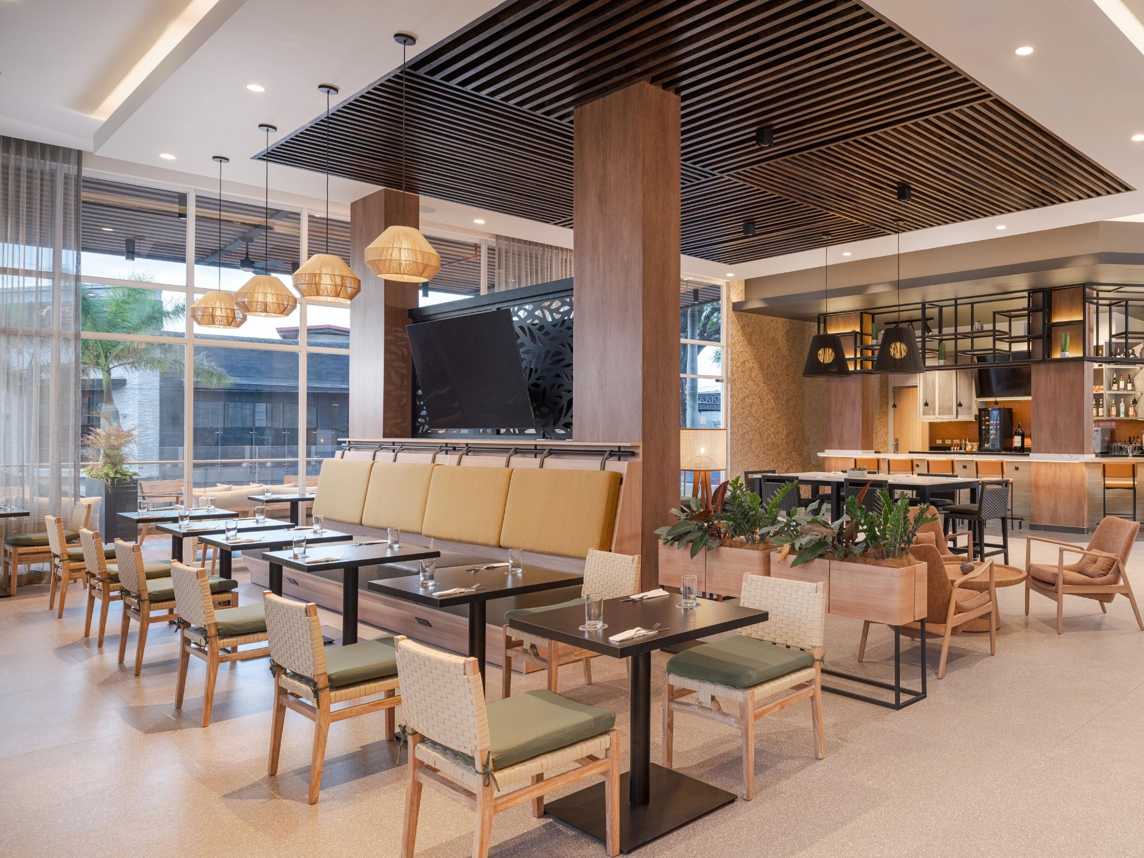 Um restaurante moderno com área de bar, janelas amplas e diversas opções de assento, incluindo mesas e cabines.