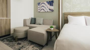 Quarto de hotel moderno com uma cama, um sofá, uma mesinha com uma planta e um objeto decorativo na parede.