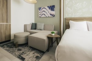 Quarto de hotel moderno com uma cama, um sofá, uma mesinha com uma planta e um objeto decorativo na parede.