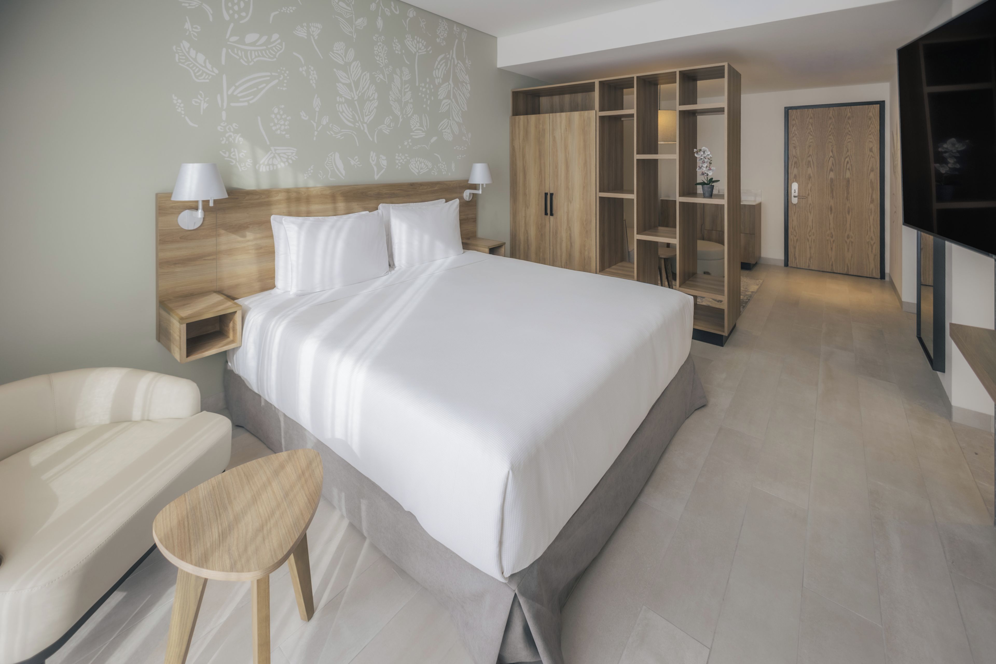 Quarto de hotel moderno com uma cama grande, guarda-roupa de madeira, área de estar e televisão.