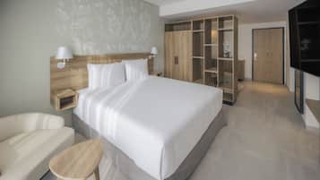 Quarto de hotel moderno com uma cama grande, guarda-roupa de madeira, área de estar e televisão.