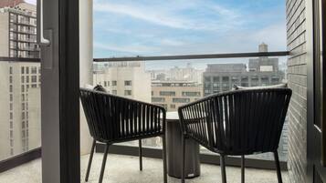 Varanda com duas cadeiras e uma mesa pequena, com vista para um horizonte urbano repleto de edifícios.