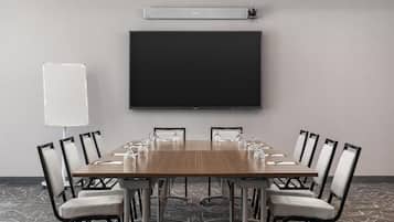Uma sala de conferências com uma grande mesa, cadeiras, uma TV de tela plana e um quadro branco.