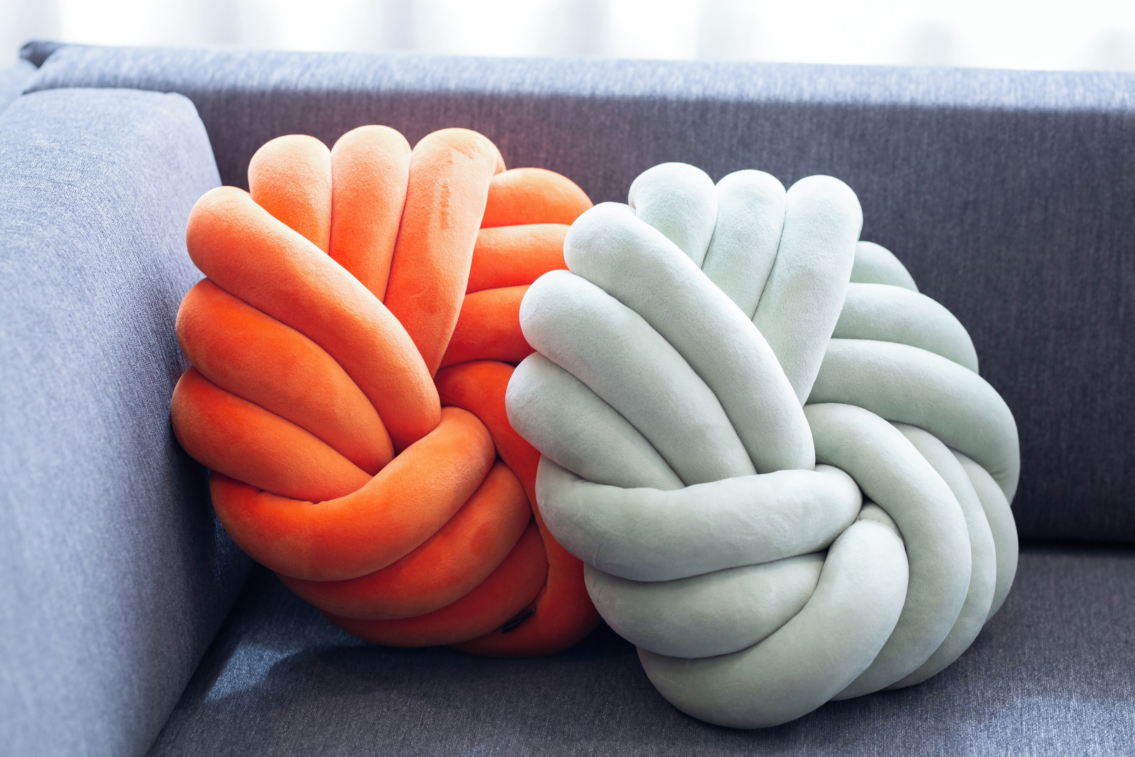 Dois pufes tricotados em laranja e branco sobre um sofá cinzento.
