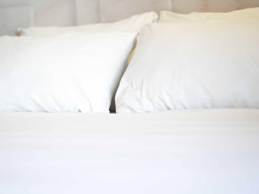Uma cama com roupa de cama e almofadas brancas.