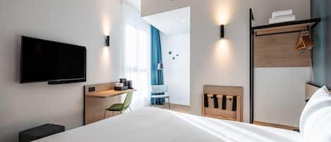 Quarto de hotel moderno com cama, televisão de tela plana, escrivaninha com cadeira, cabeceira de madeira e televisão fixada na parede.