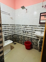 Um banheiro pequeno com vaso sanitário, um balde vermelho, pia e chuveiro.