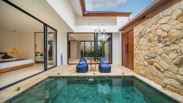 Uma área de piscina moderna com um muro de pedra, dois assentos de poliuretano azul e vista para o exterior.