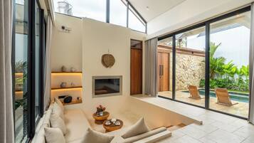 Uma sala de estar moderna com sofá, mesa de centro e televisão de tela plana. Há uma parede de pedra e vista para uma piscina externa.