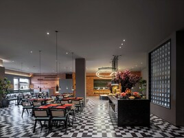 Um restaurante moderno com piso xadrez, várias mesas de jantar e um lustre decorativo central.