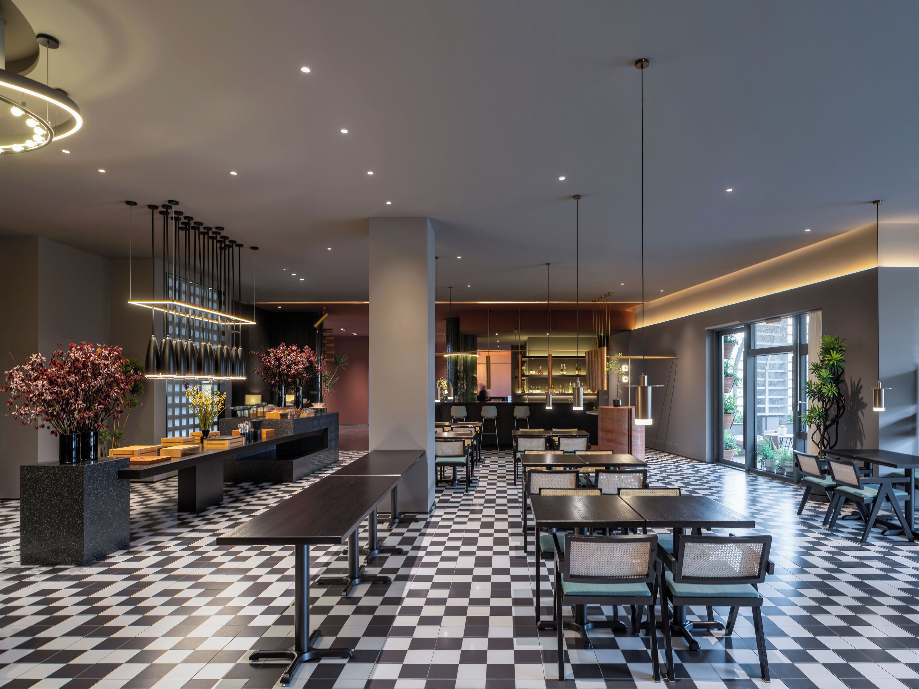 Um restaurante moderno com piso xadrez, iluminação pendente em preto e branco, e uma área de bar ao fundo.