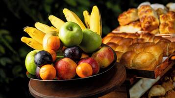 Uma tigela de frutas com maçãs, laranjas e bananas, e uma travessa de pão.