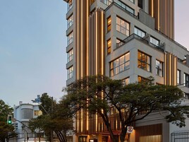 Um edifício moderno de grande altura, com vários andares, janelas amplas e uma marcante estrutura de iluminação vertical.