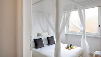 Cama com dossel, paredes brancas, uma mesinha com bandeja e uma janela.