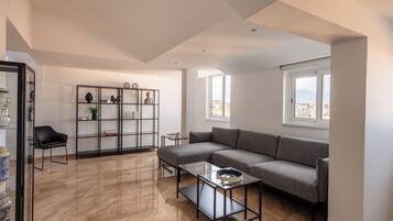 Uma sala de estar moderna com sofá seccional, mesa de centro de vidro, cadeira preta e estante com objetos decorativos.