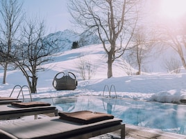 Área de piscina com espreguiçadeiras e uma cadeira esférica incomum, emoldurada por uma paisagem coberta de neve e árvores.